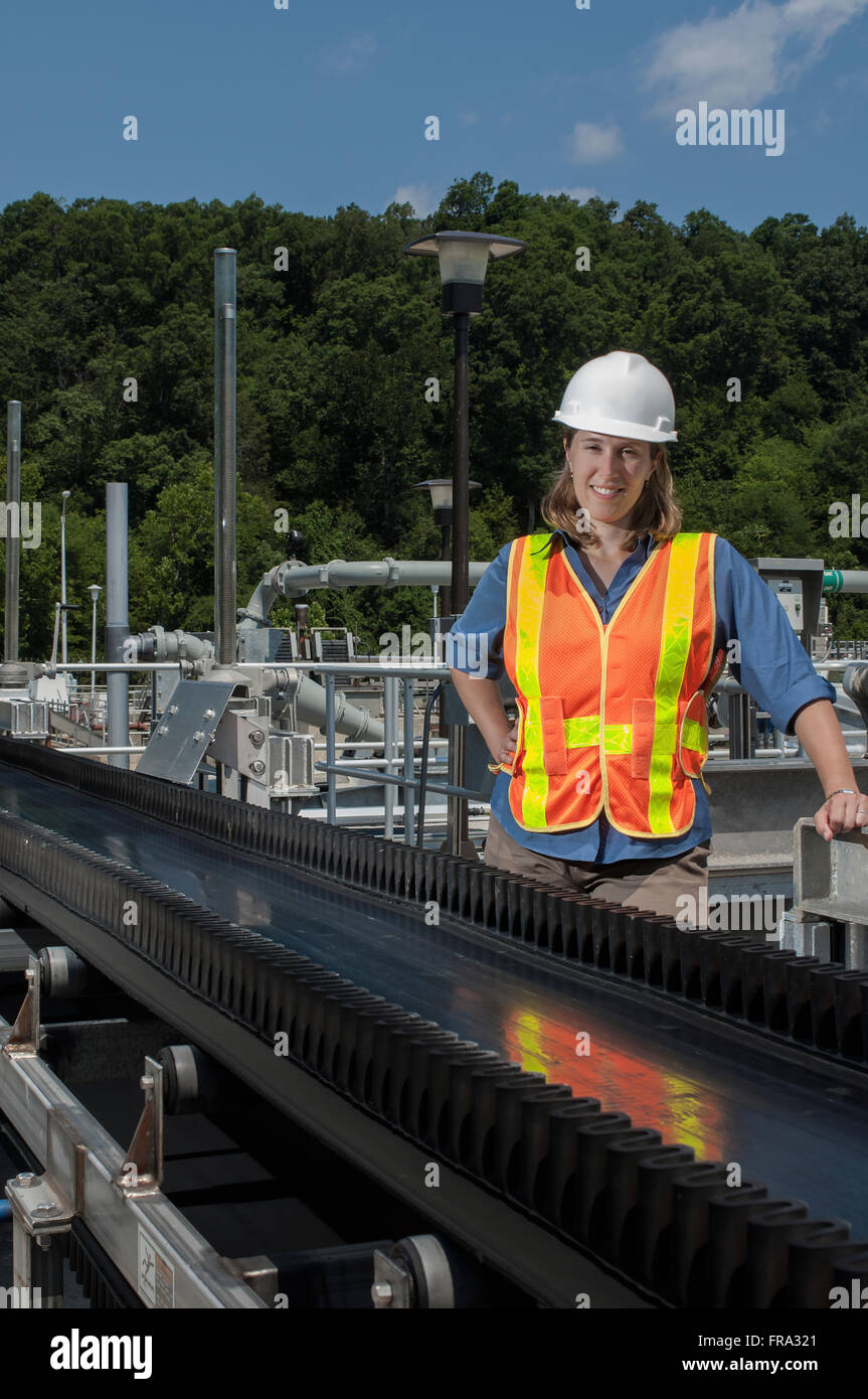 A female civil engineer, wearing a hard hat and a reflective orange ...
