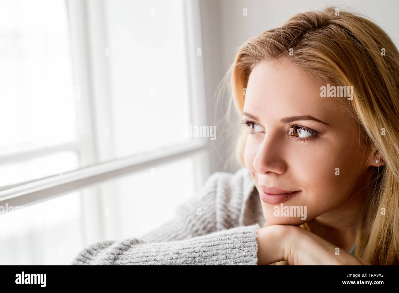 Woman sitting on window sill, looking out of window Stock Photo - Alamy