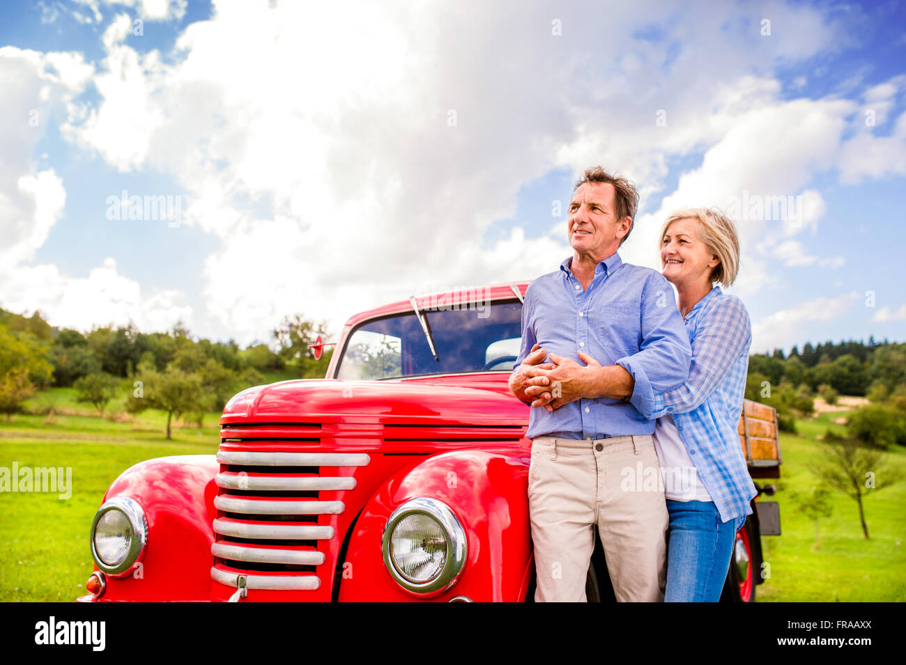 Senior couple hugging, vintage styled red car, sunny nature Stock Photo ...