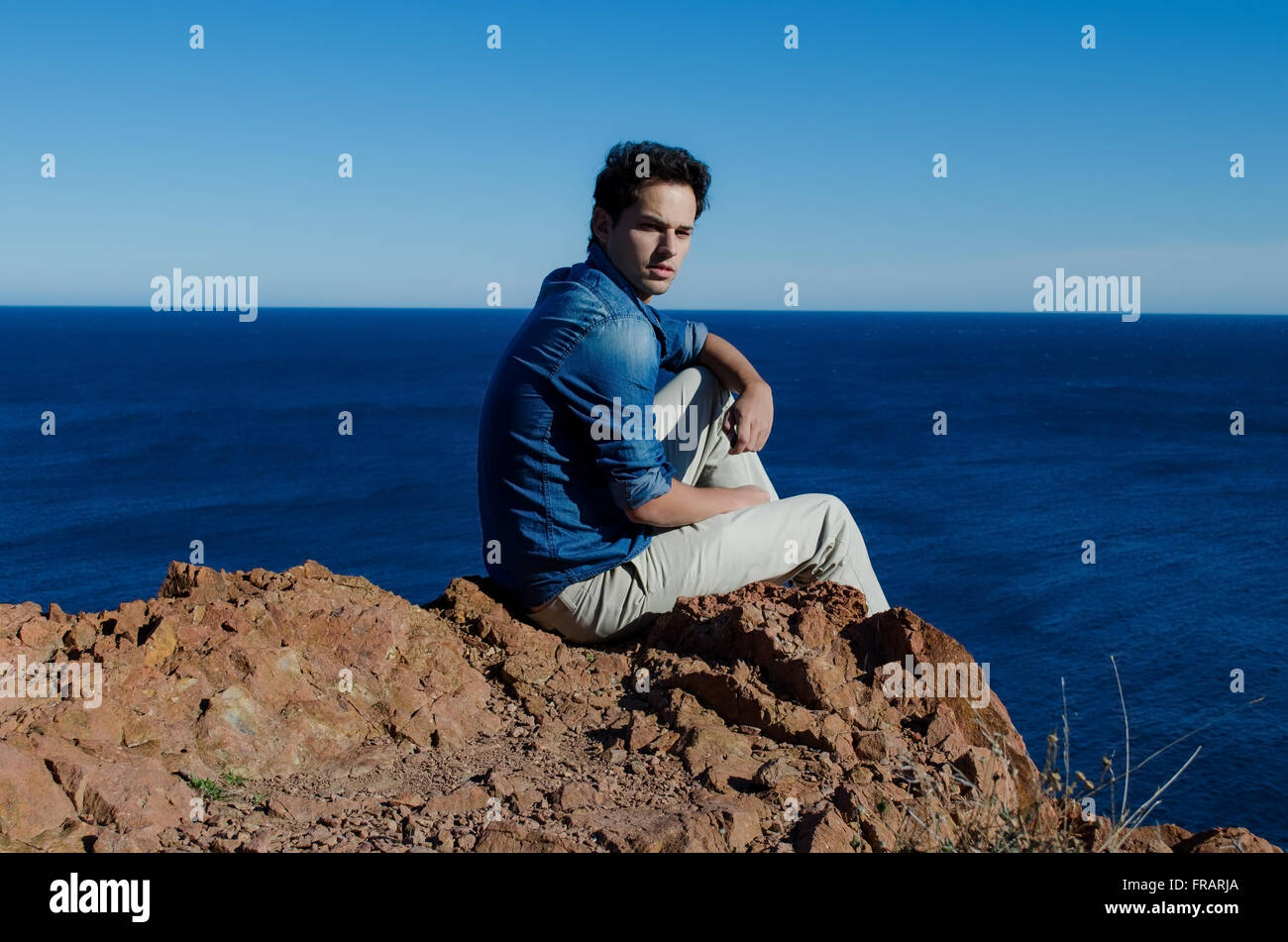 A man sitting on a rock and looking at the camera Stock Photo - Alamy