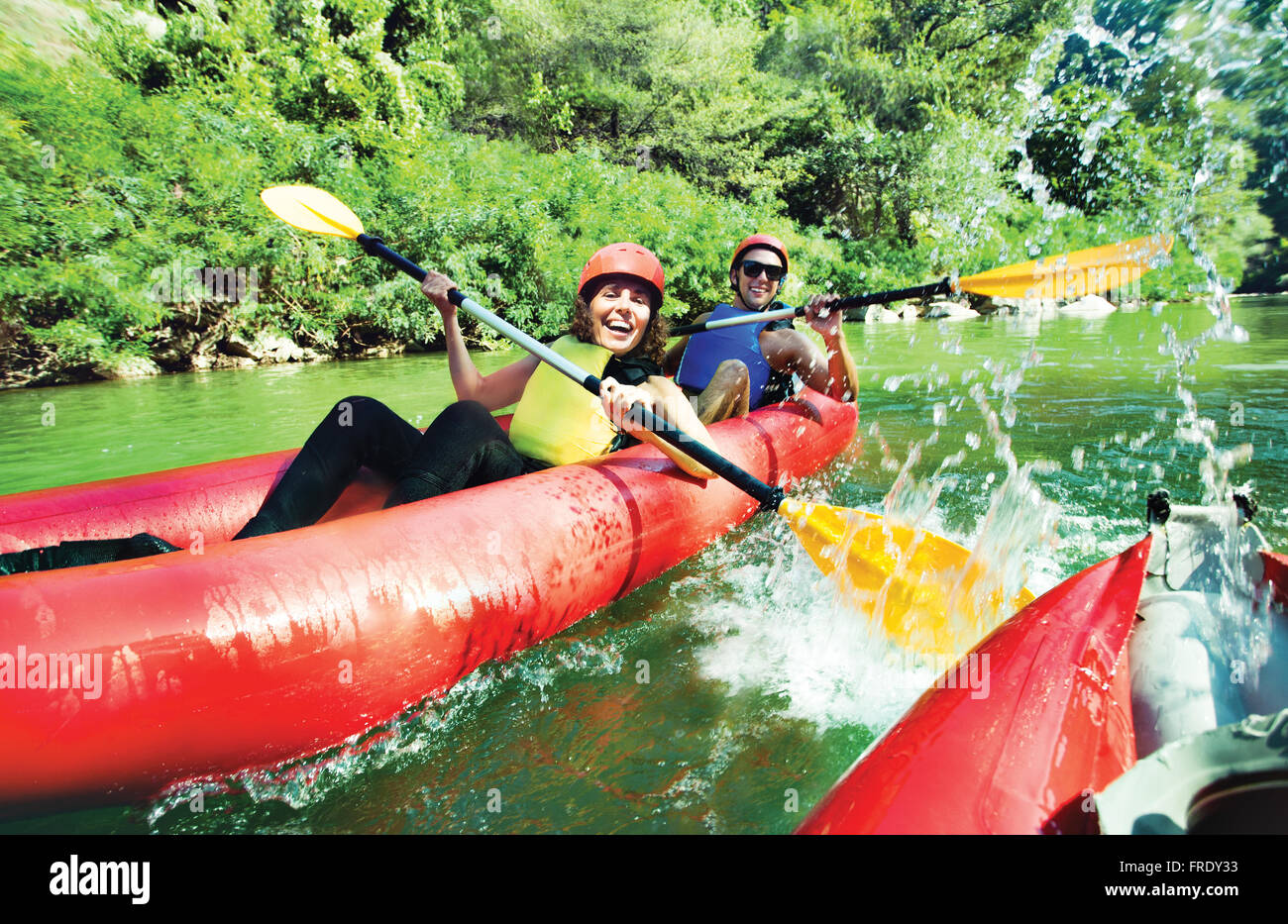 A female and a male in red inflatable canoe having fun splashing over ...