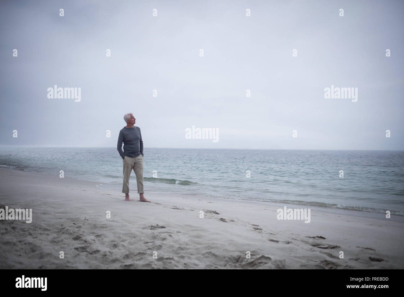 Thoughtful retired man standing on the beach Stock Photo - Alamy