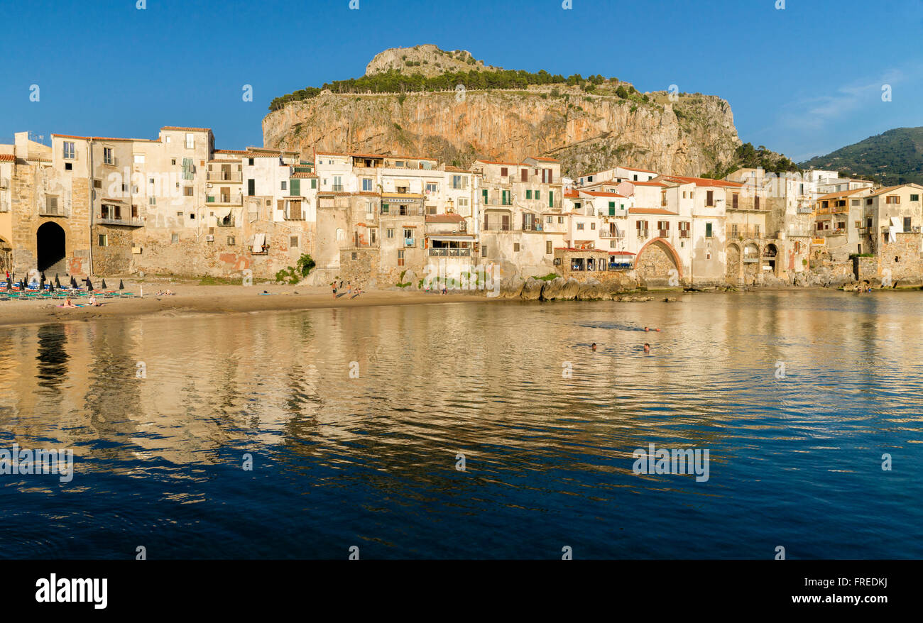 Beach in the historic centre, behind Rocca di Cefalu limestone rock ...