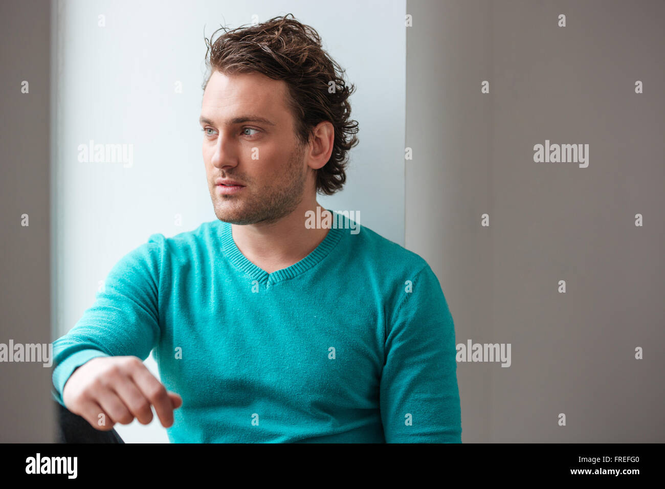 Handsome pensive young man sitting and looking at the window over white ...