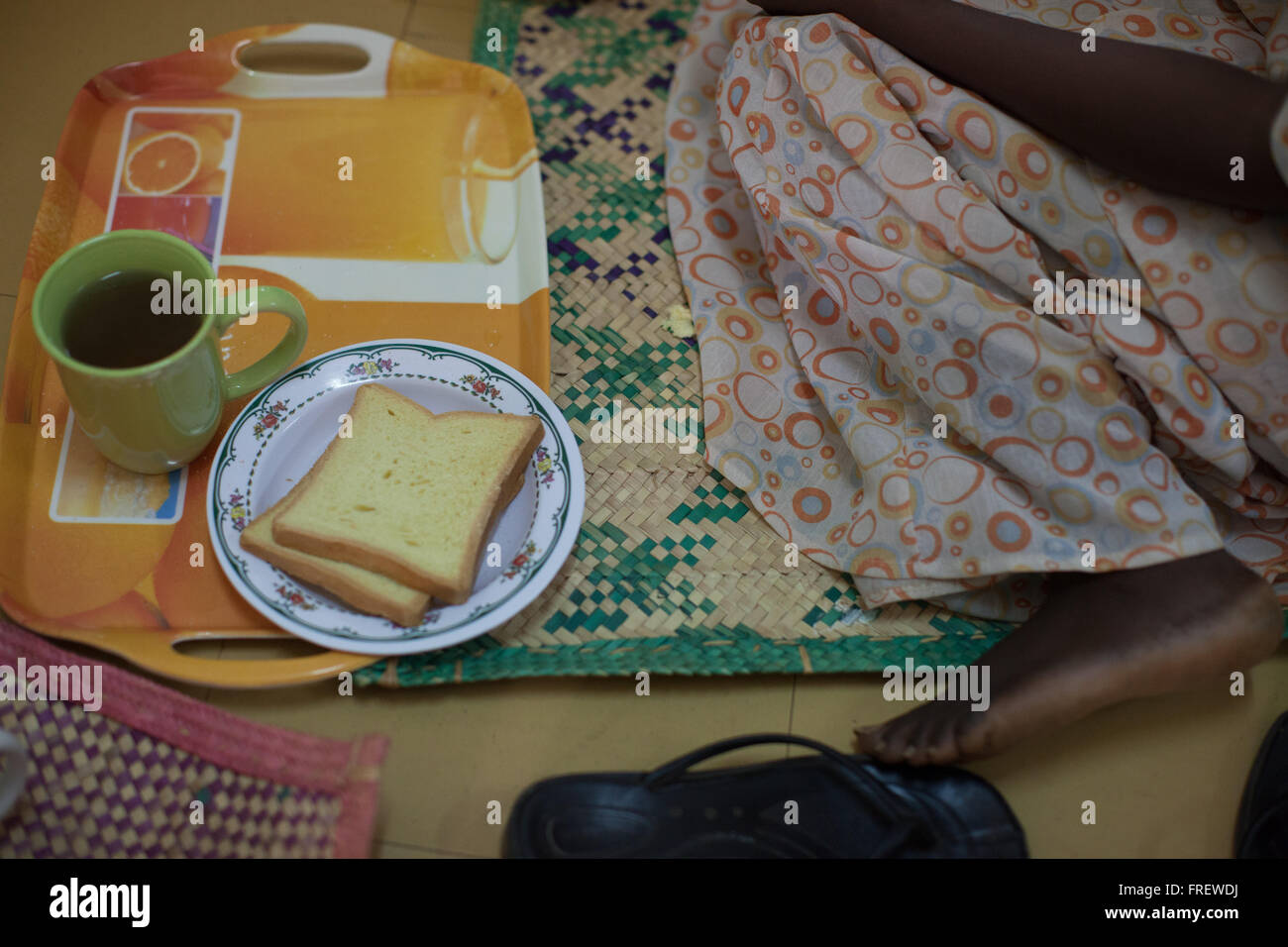 A woman lying on the floor in hospital, Uganda with tea and toast on a ...