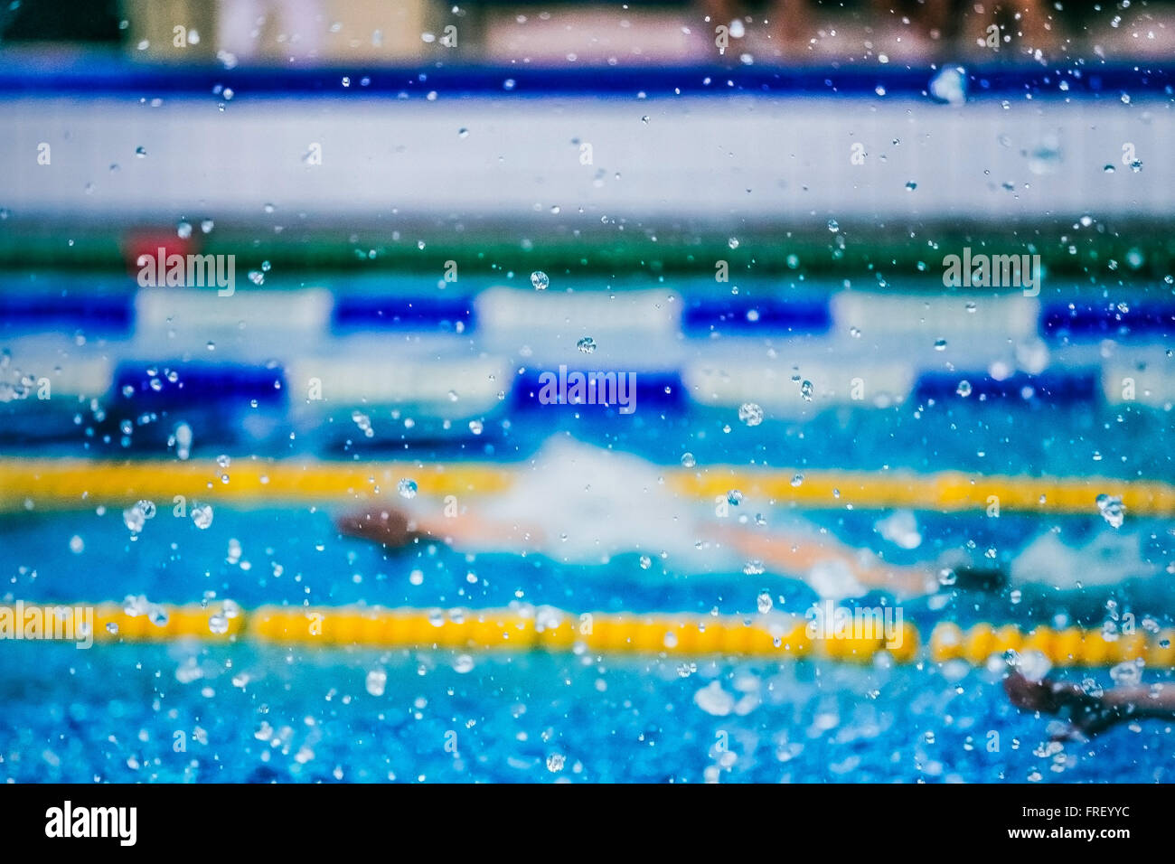 water drops on glass lens. blur effect. in background pool, and swimmer ...
