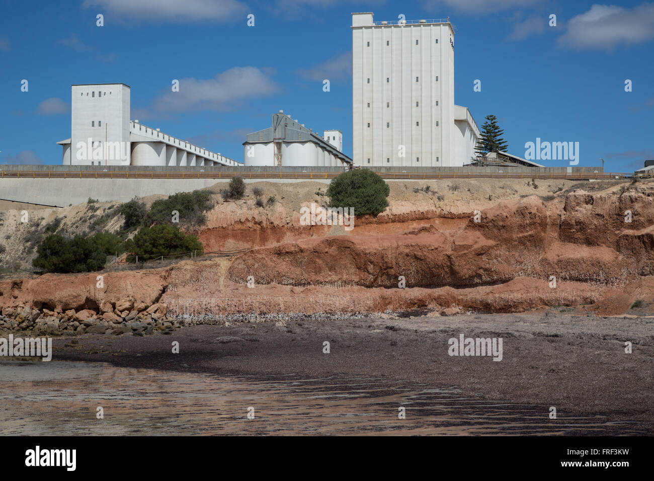 white crop storage silo facilities on top of sea shore brim with muddy ...
