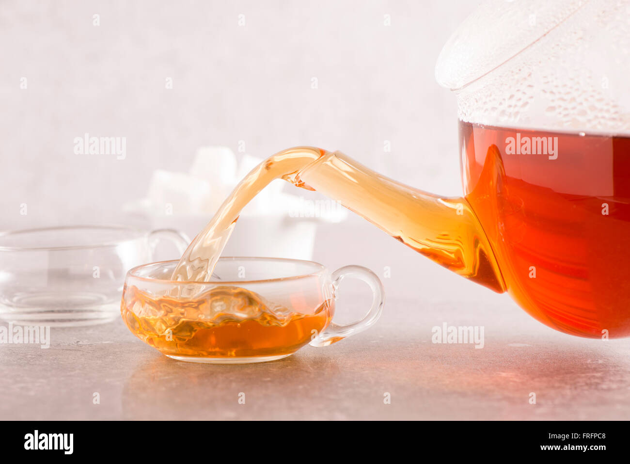 Hot tea pouring in teacup from glass teapot. Modern kitchen with stone ...