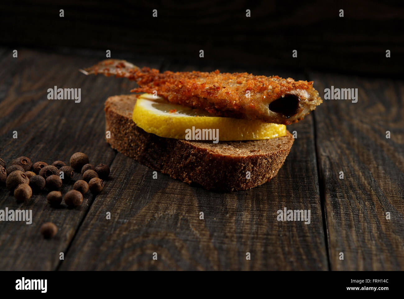 sandwich of rye bread with fried fish and lemon on a wooden background ...
