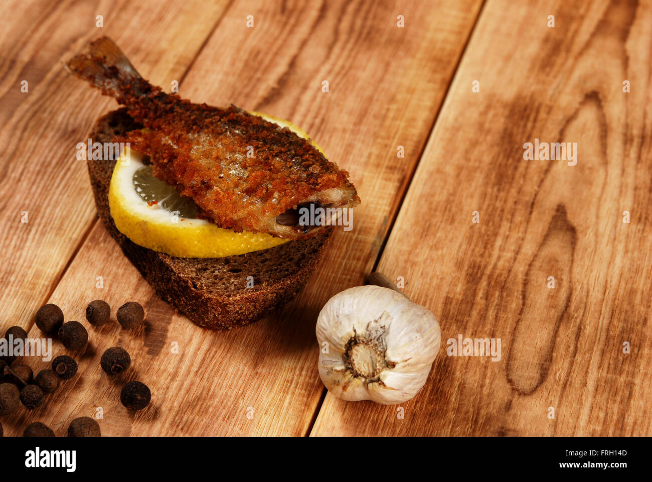 sandwich of rye bread with fried fish and lemon on a wooden background ...