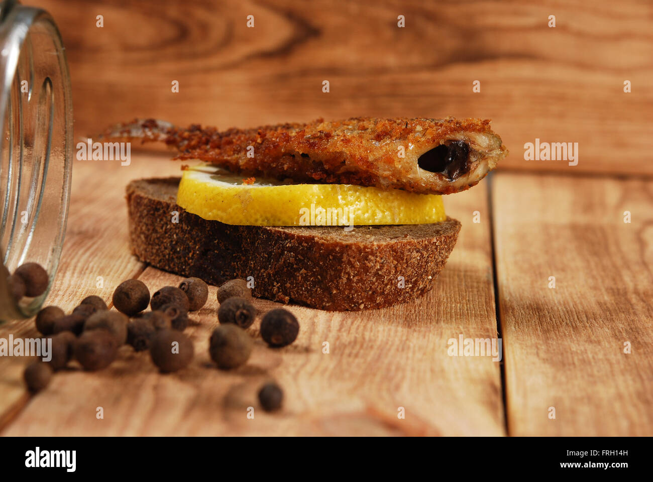 sandwich of rye bread with fried fish and lemon on a wooden background ...