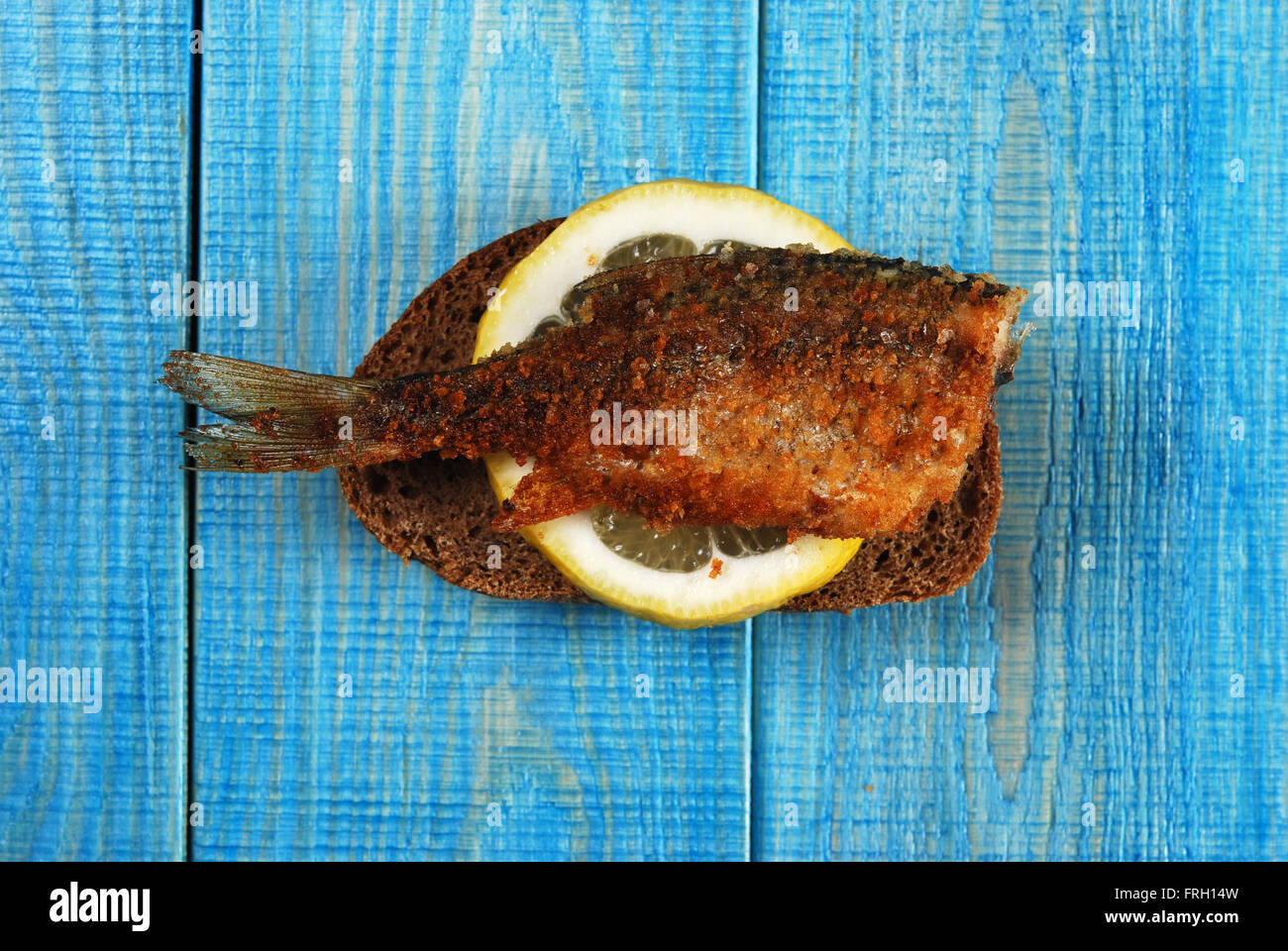 sandwich of rye bread with fried fish and lemon on a blue wooden ...