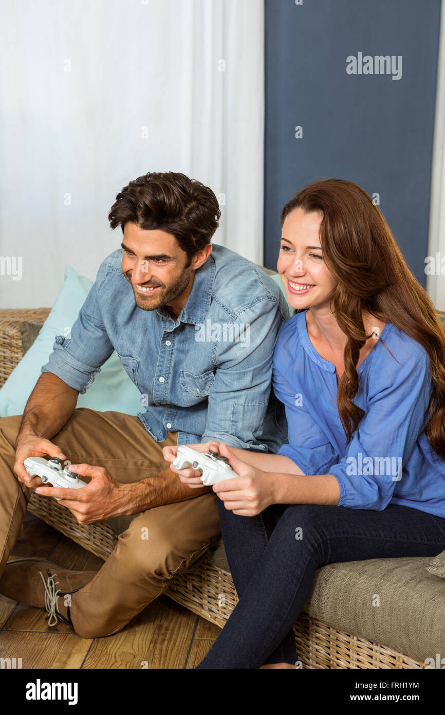 Young couple playing video game while sitting on sofa Stock Photo - Alamy