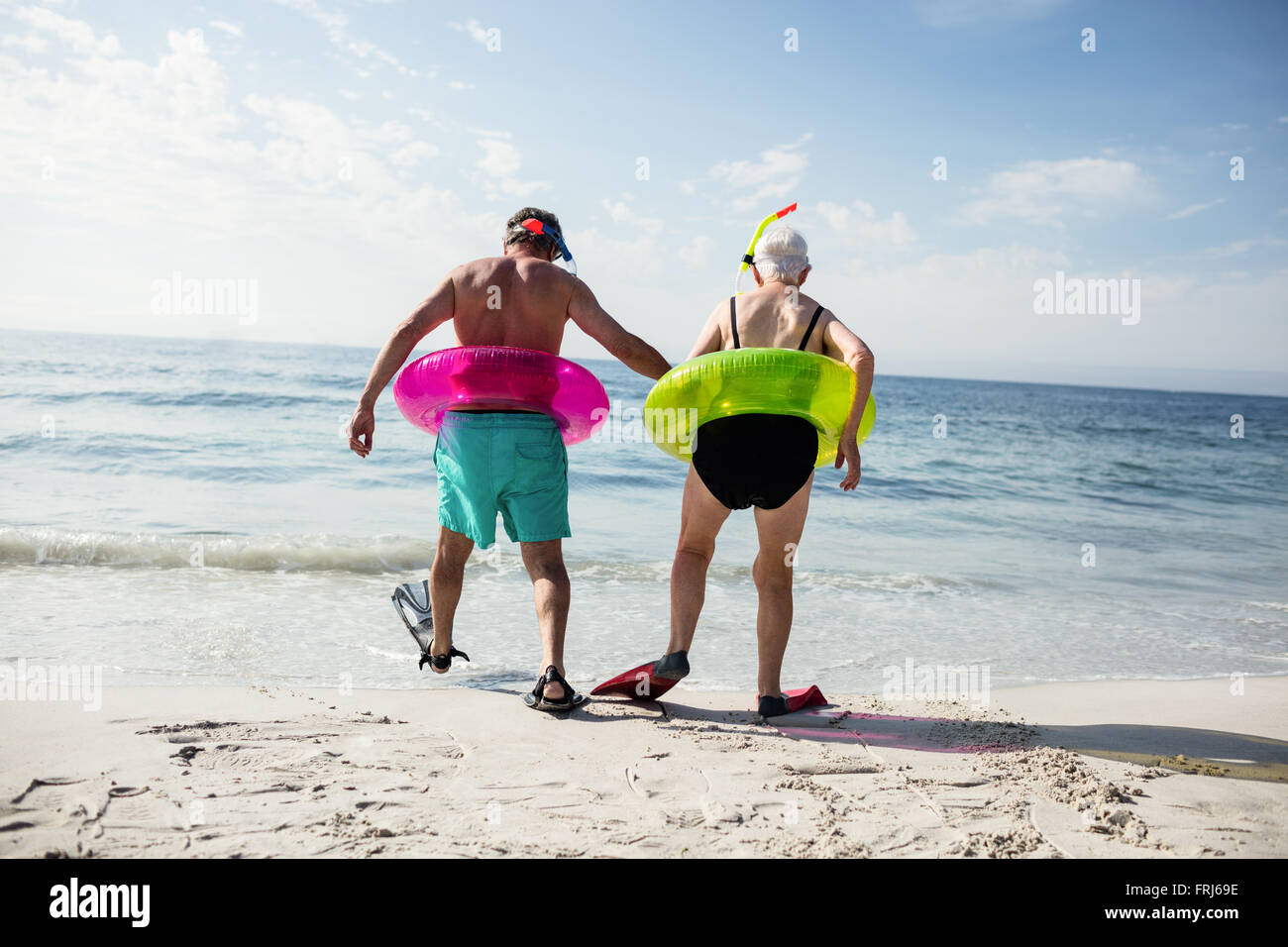 Senior couple in inflatable ring and flipper walking towards sea Stock ...