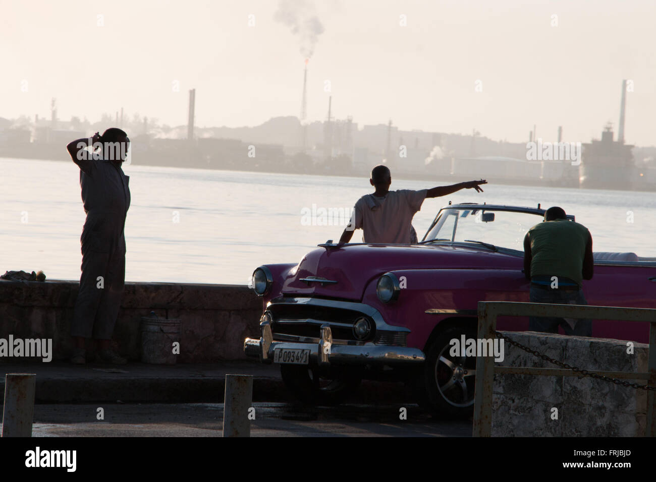 Taxi being washed in Havana with plumes of pollution in the background ...
