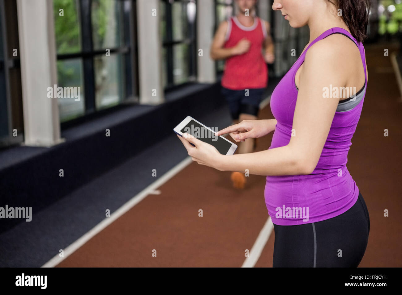 Trainer using a digital tablet while man performing running exercise ...