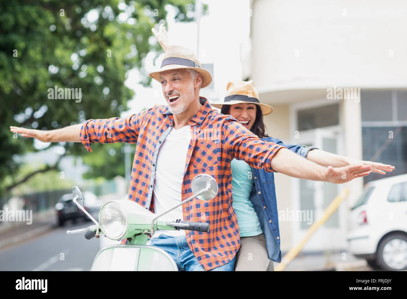 Couple riding moped with arms outstretched Stock Photo - Alamy