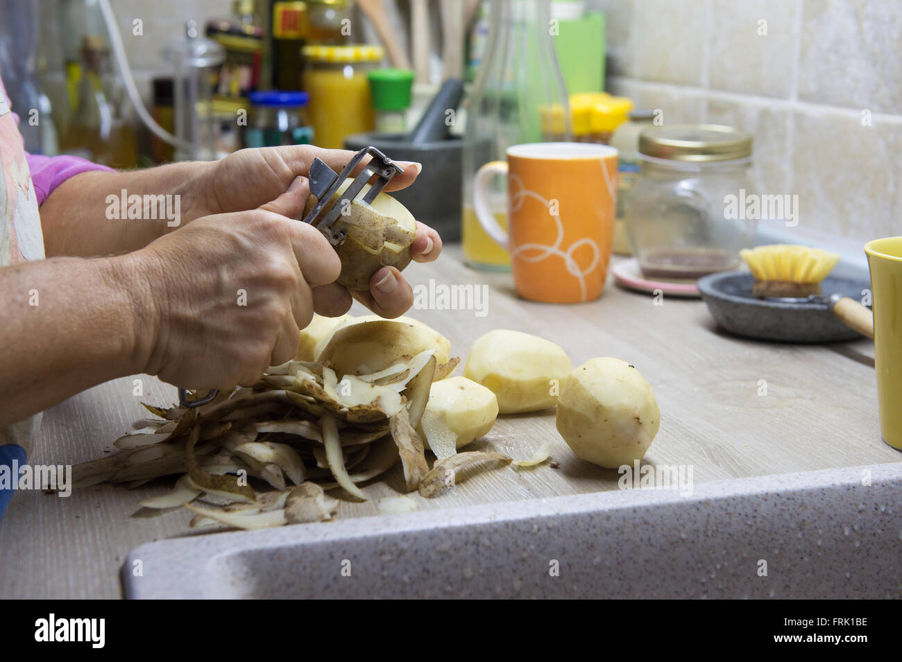Woman peeling potatoes in the kitchen next to the sink. Organic ...