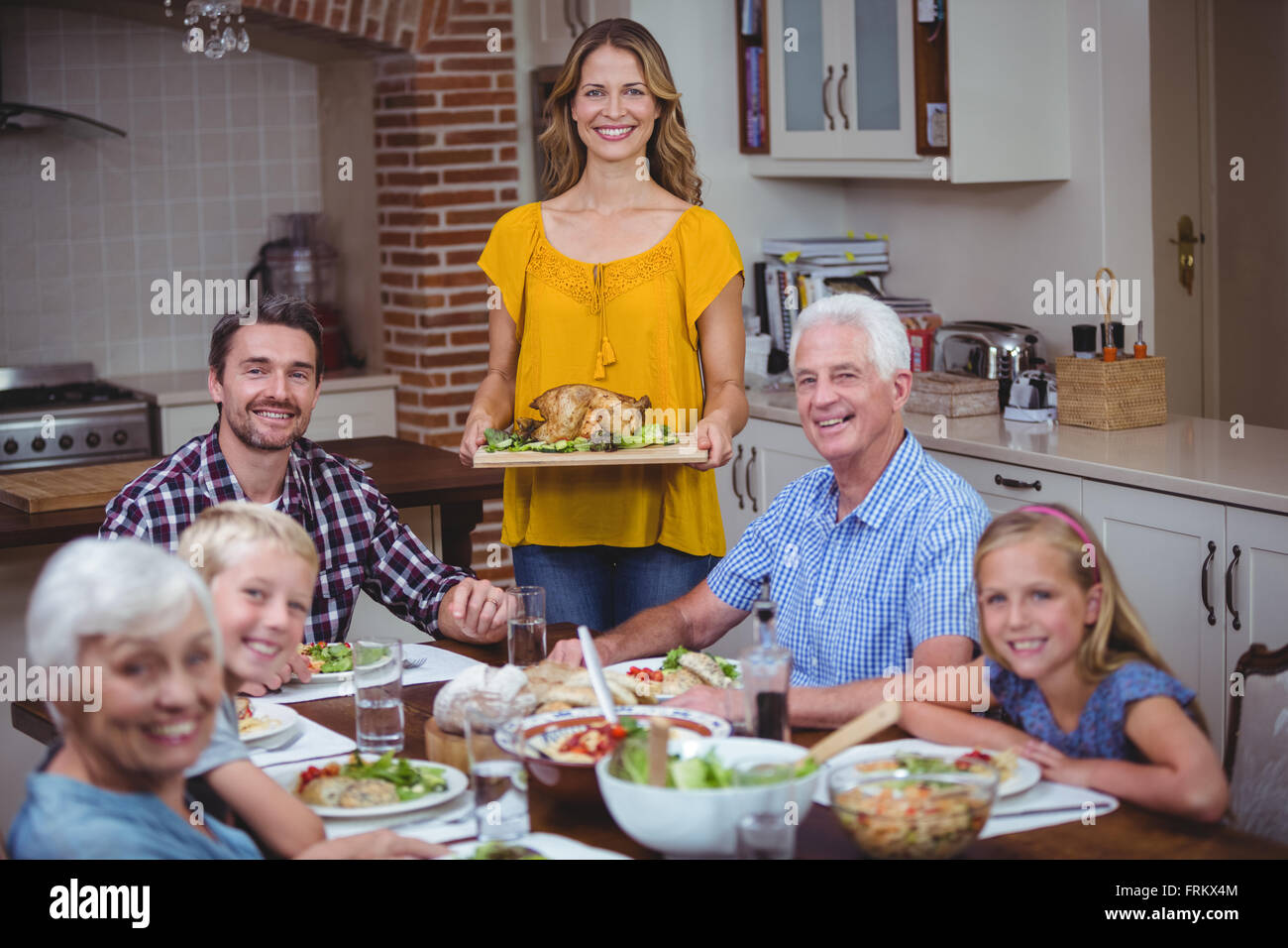 Smiling family at dining table with mother standing Stock Photo - Alamy
