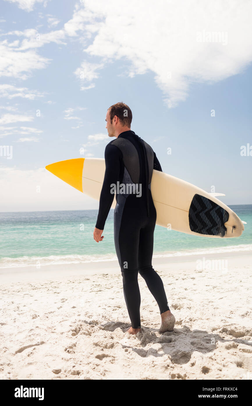 Rear view of surfer with surfboard standing on the beach Stock Photo ...