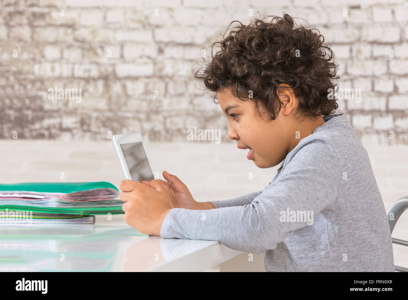 Little school boy smiling while using digital tablet at homework desk ...