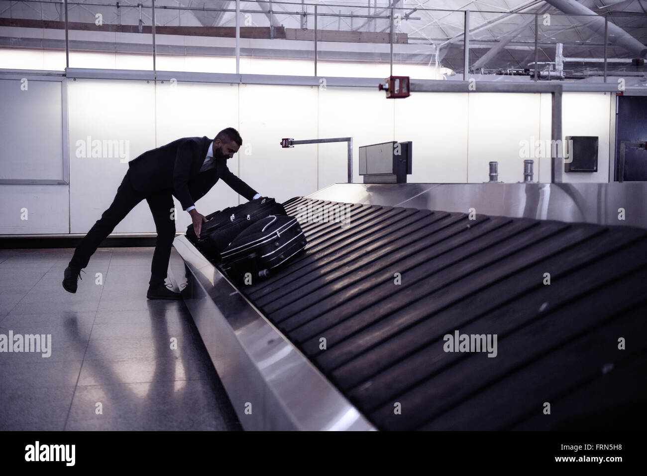 Businessman picking up suitcase on luggage conveyor belt, airpor Stock ...