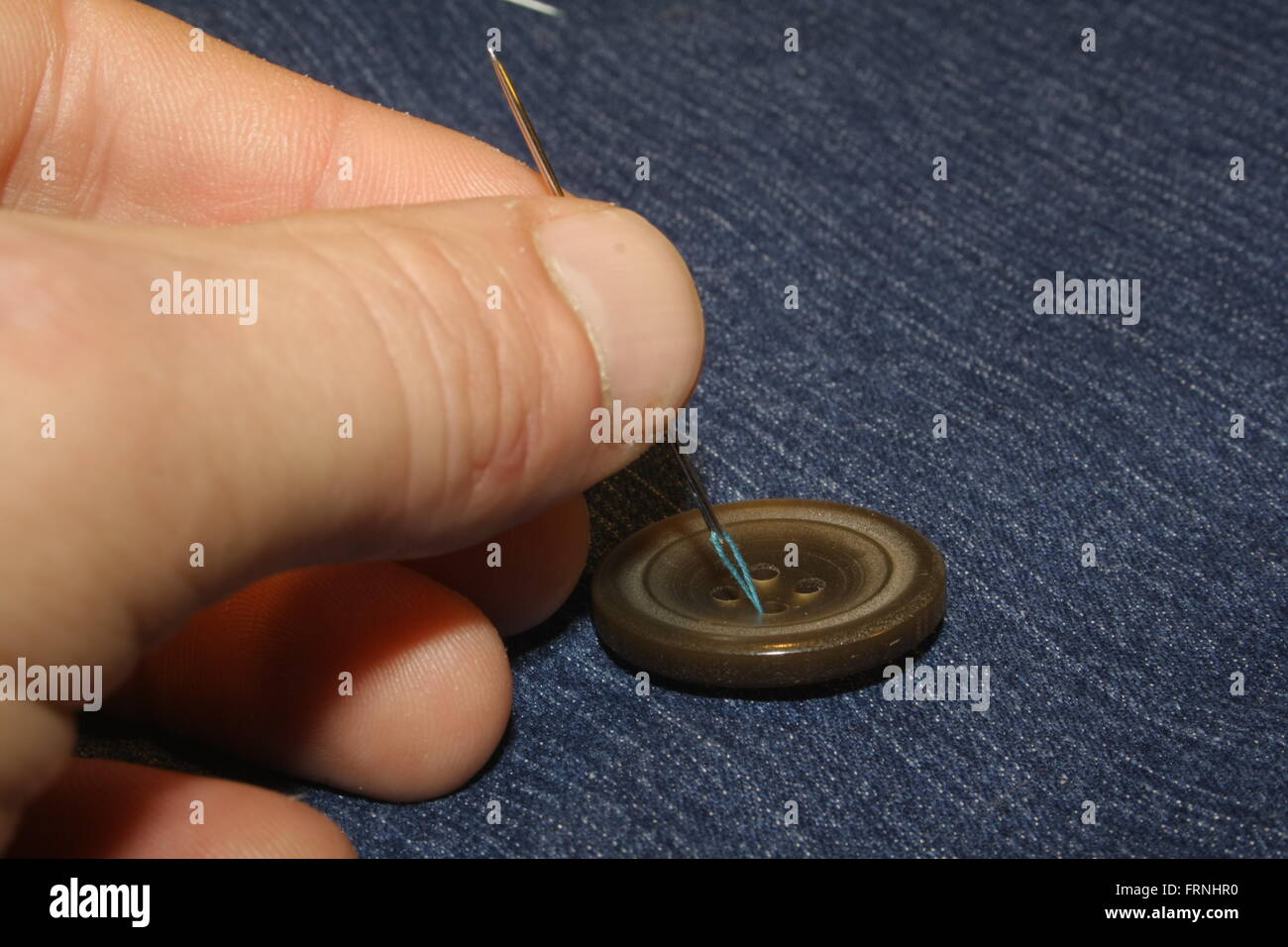 sewing a button to blue cloth Stock Photo - Alamy