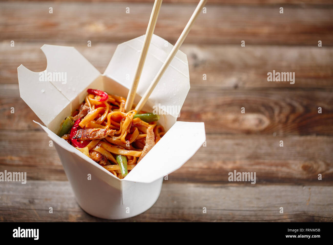 Noodles with pork and vegetables in take-out box on wooden table Stock ...