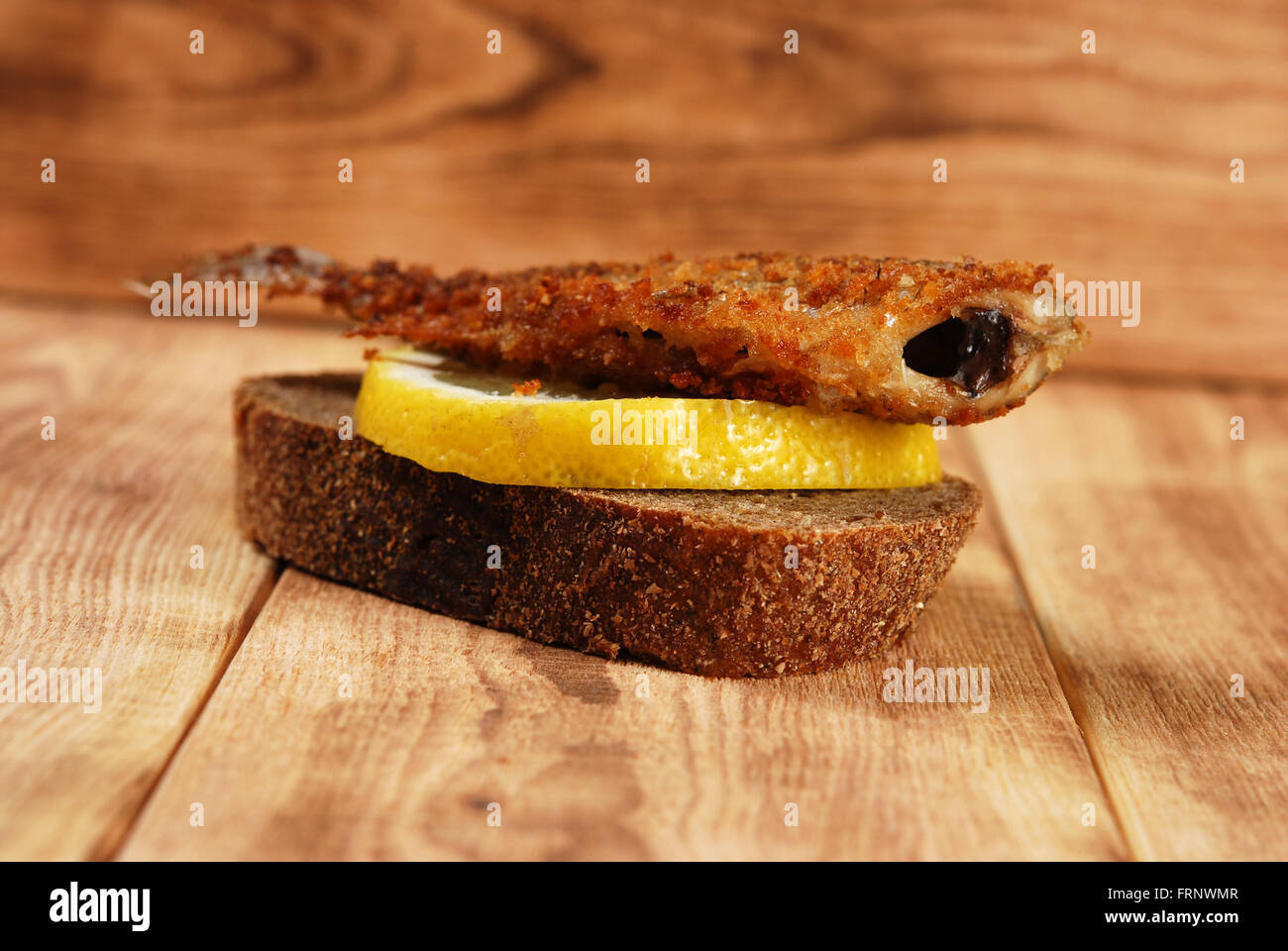 sandwich of rye bread with fried fish and lemon on a wooden background ...