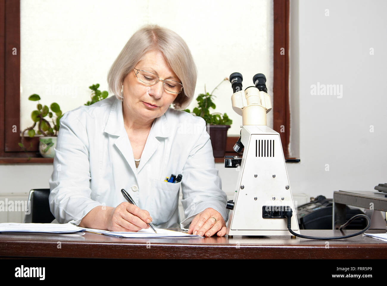 Female doctor in office with microscope writing horizontal Stock Photo ...