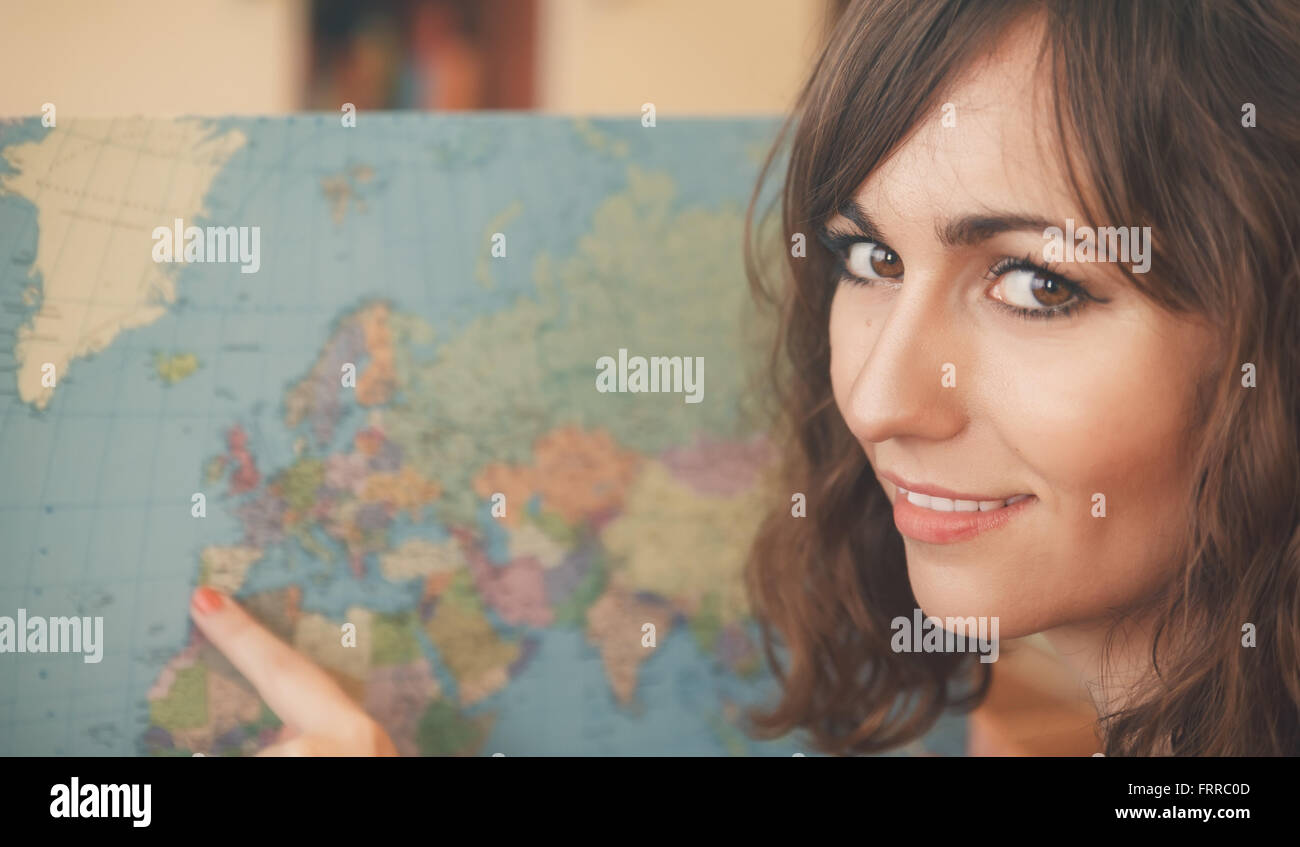 Attractive woman holding a world map turning to smile at the camera as ...