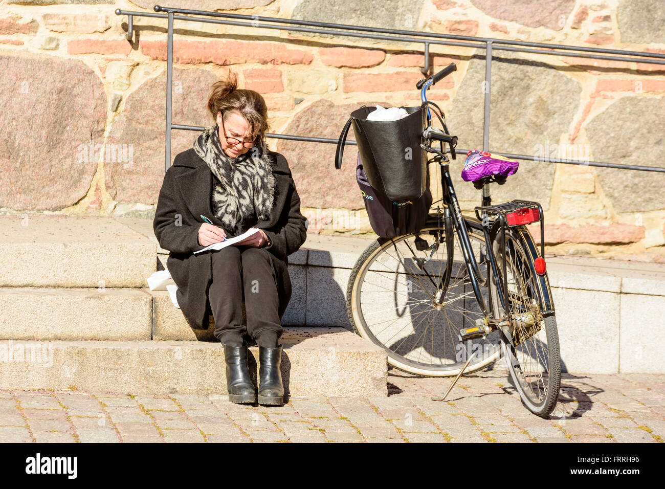 Kalmar, Sweden - March 17, 2016: A woman sit beside a bike writing in a ...