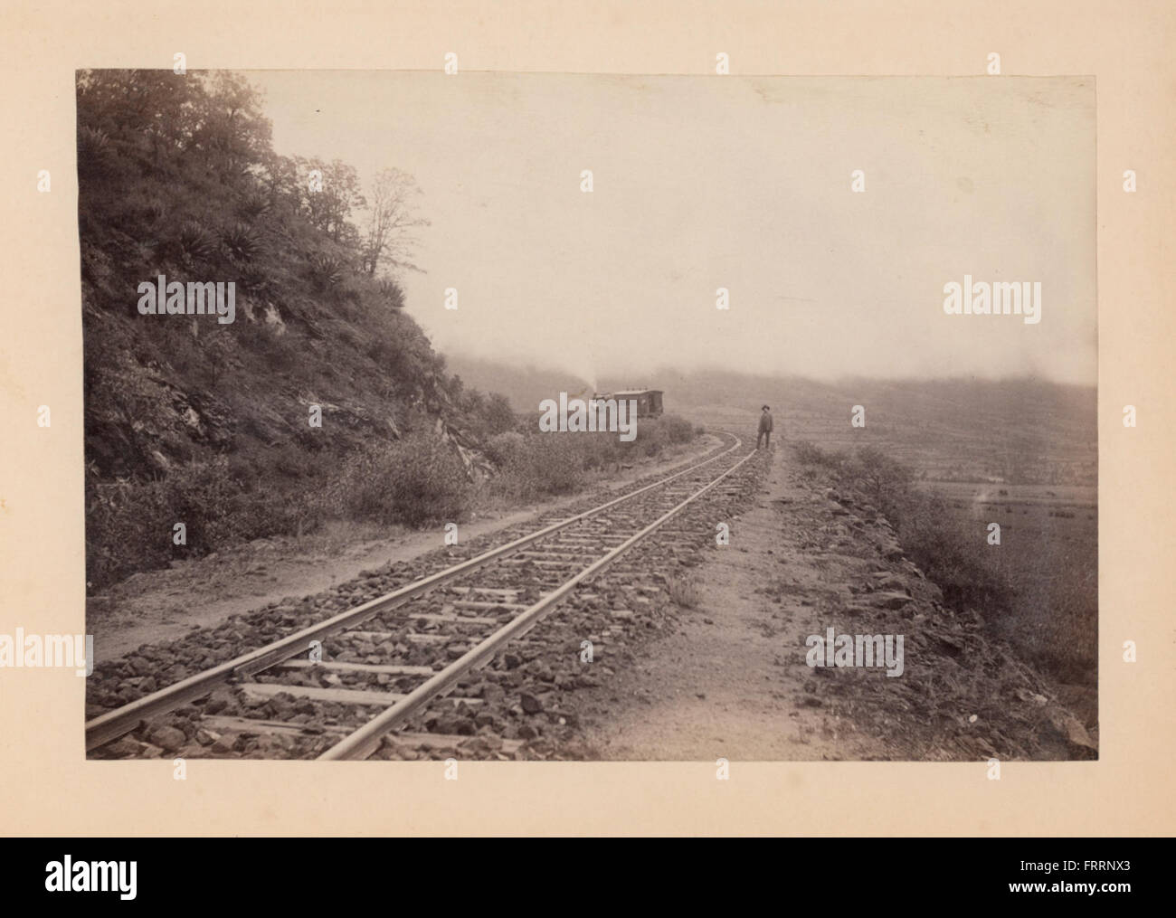 A photograph showing a man standing next to railroad tracks with a ...