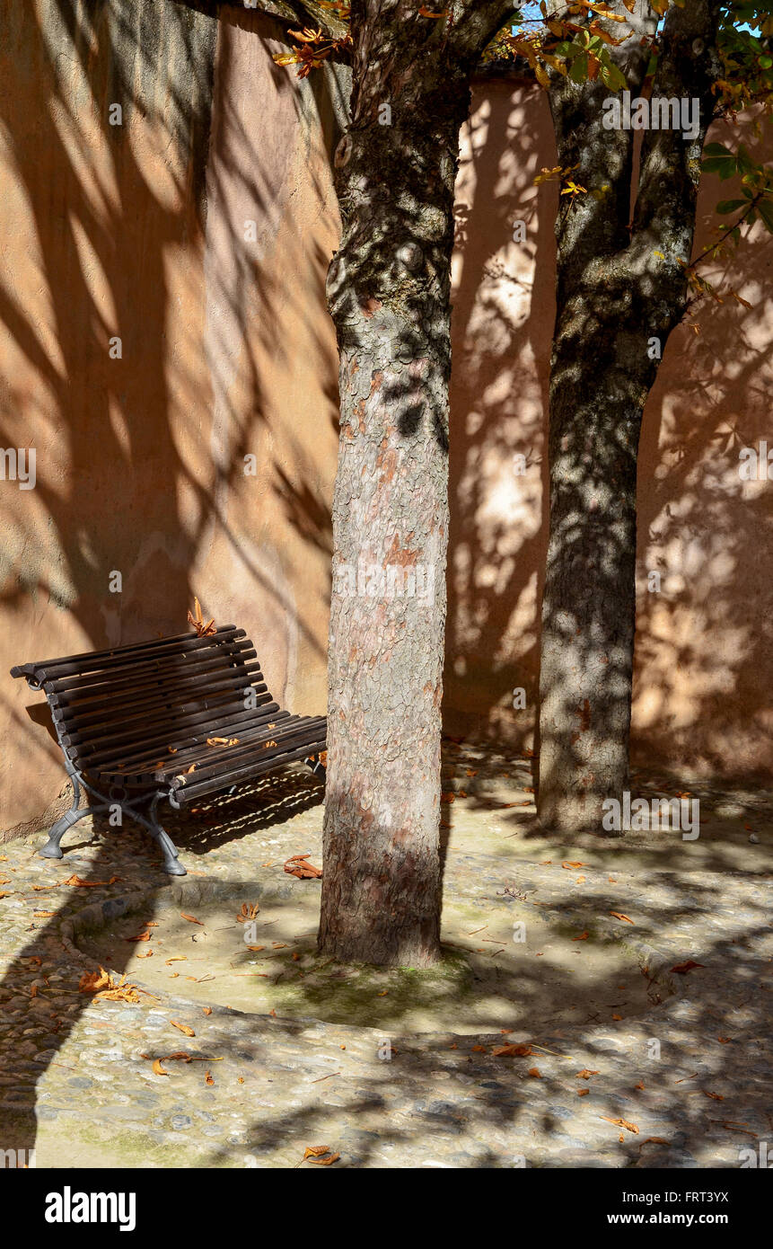 Seating bench, trees and wall in shadow and bright sunshine in the ...