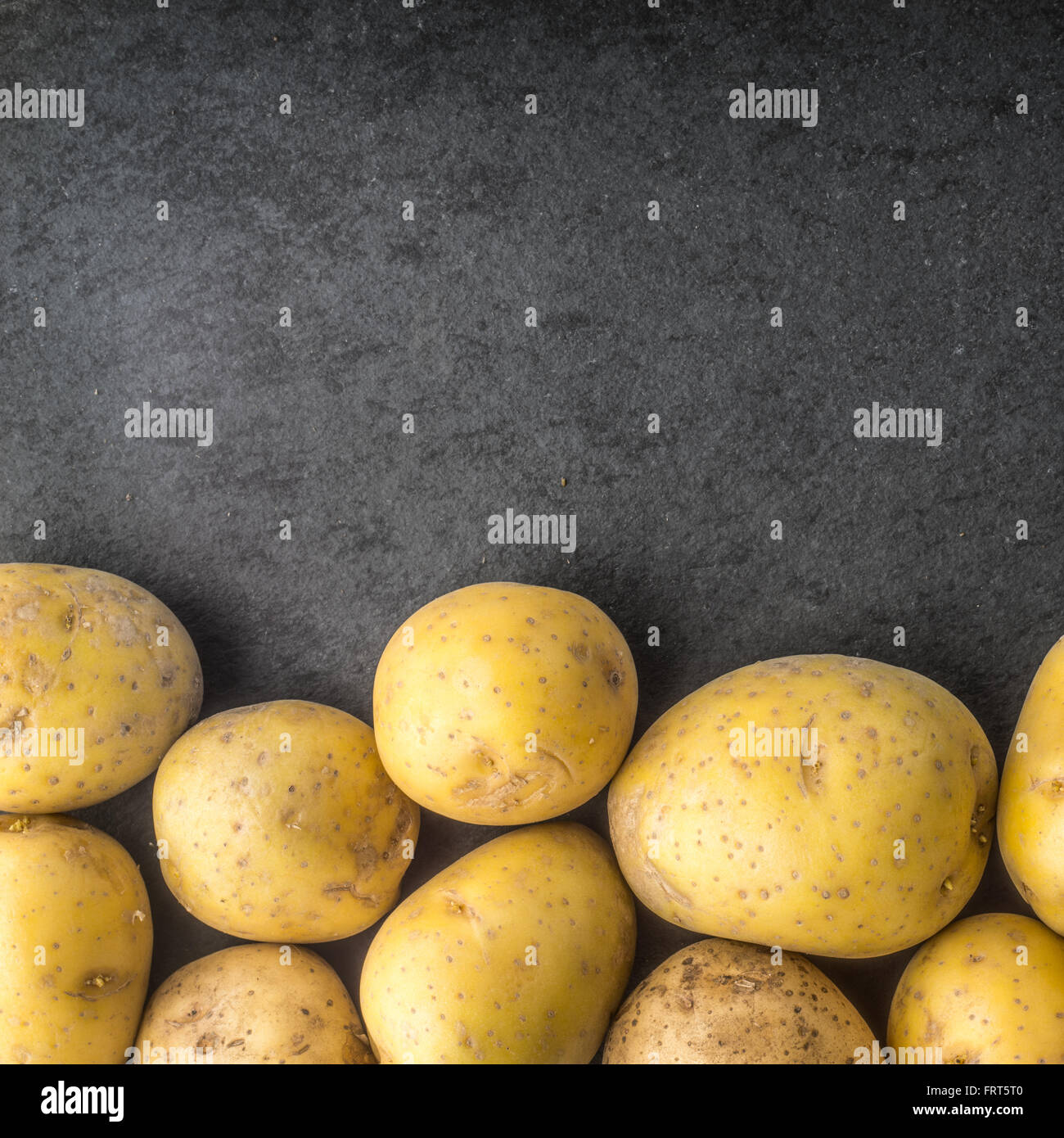 Raw potatoes on the black stone table square Stock Photo - Alamy