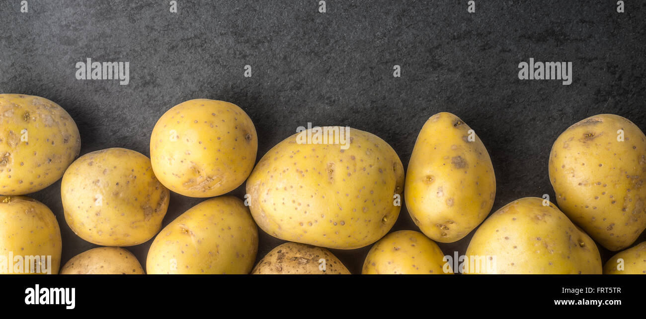 Raw potatoes on the dark stone table wide screen Stock Photo - Alamy