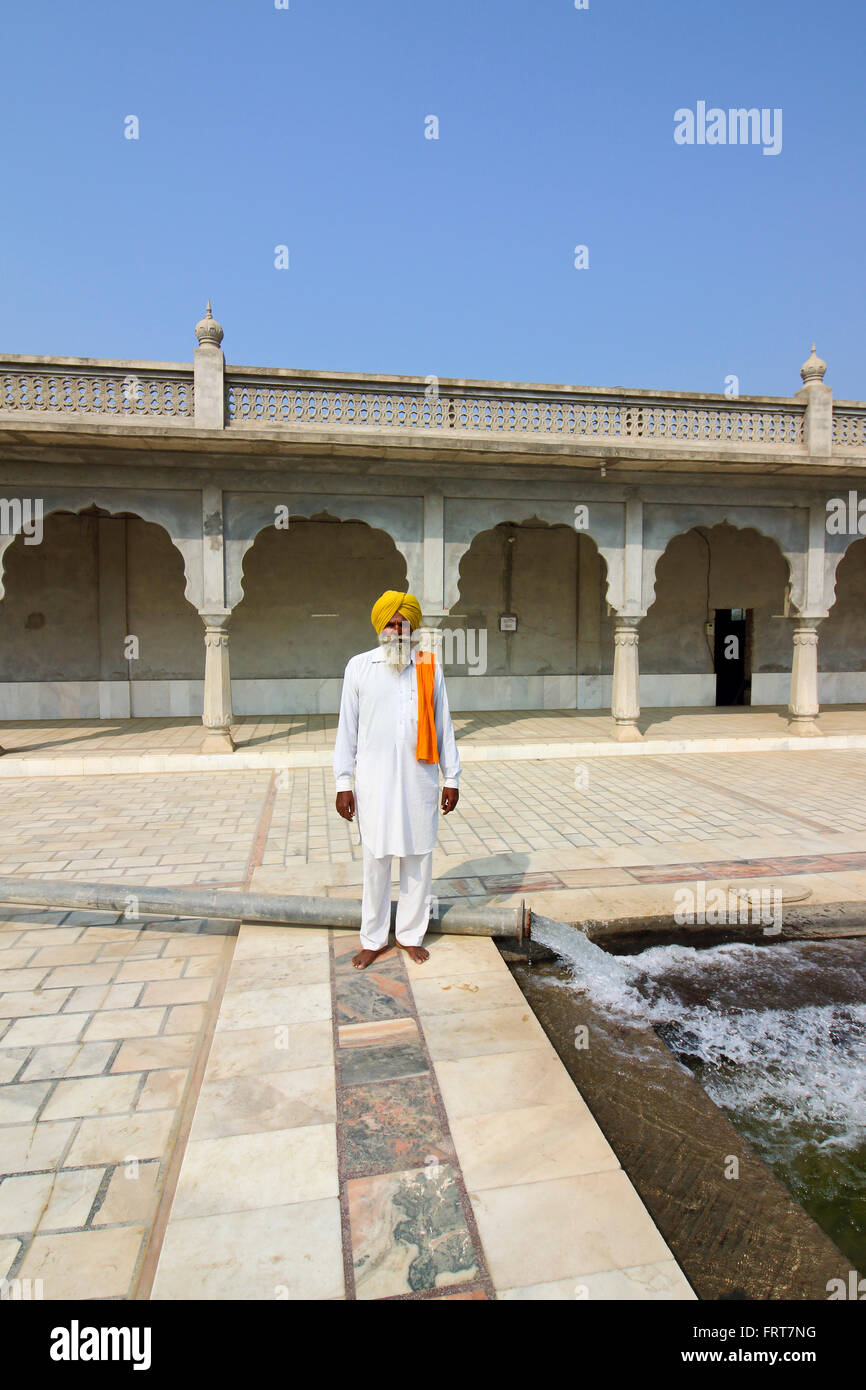 A Sikh elder with a yellow turban and white salwar kameez filling the ...