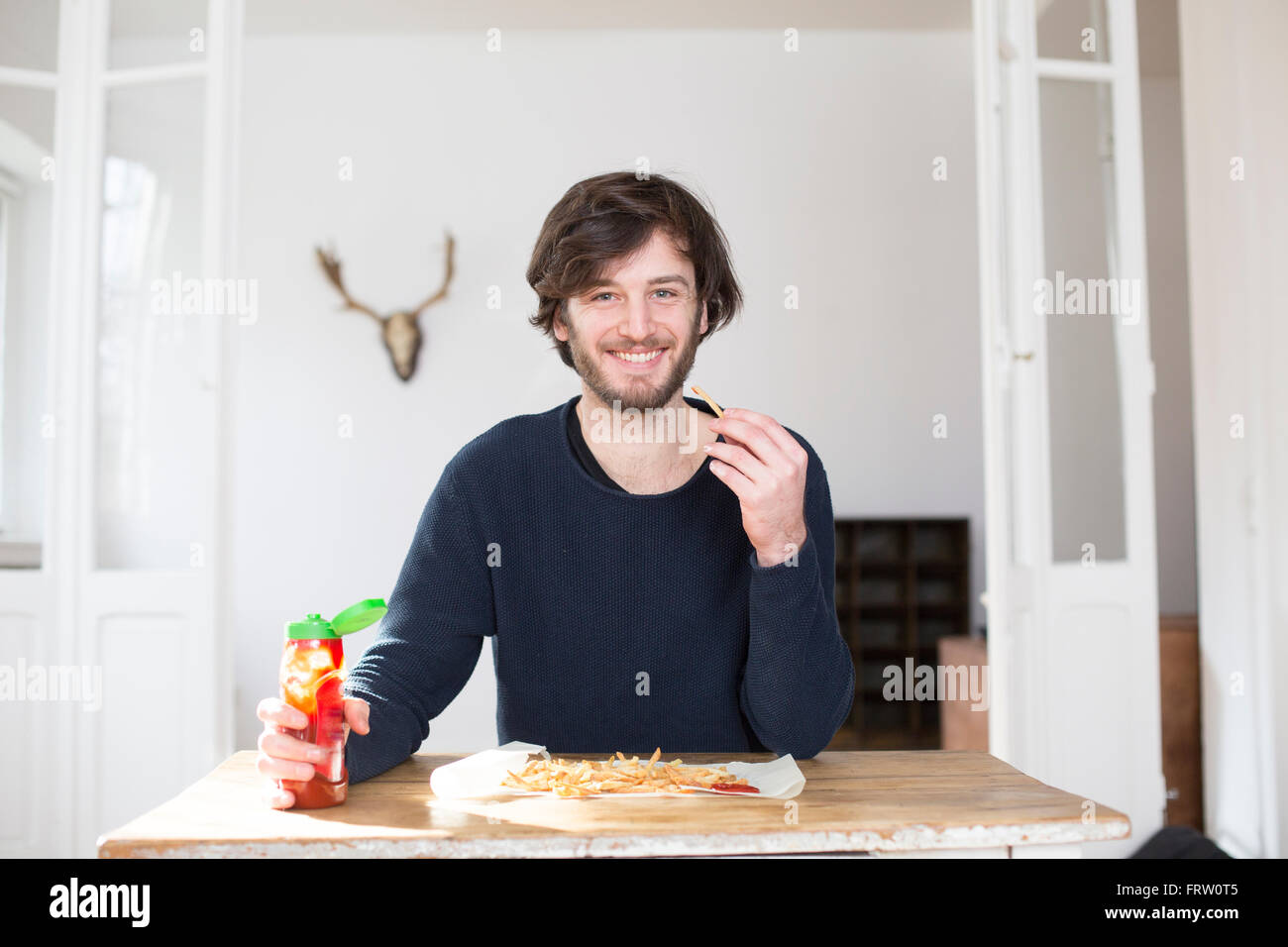 Portrait of smiling young man eating French fries with ketchup Stock ...