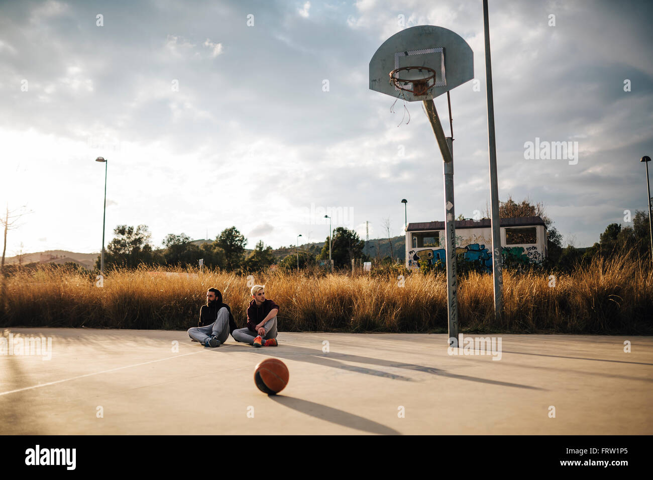 Two young men sitting on outdoor basketball court Stock Photo - Alamy