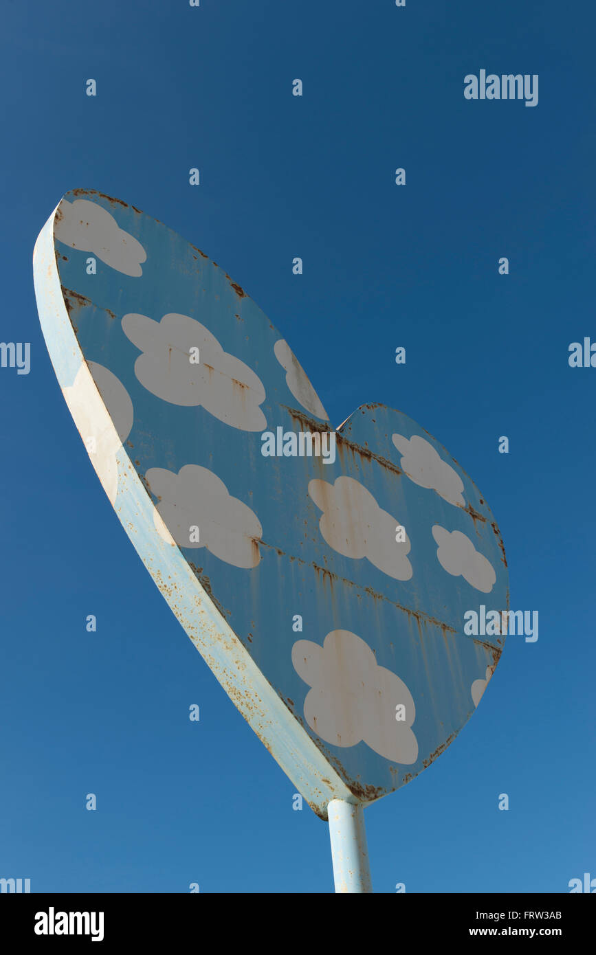 Rusty light blue metal heart with white clouds in front of blue sky ...