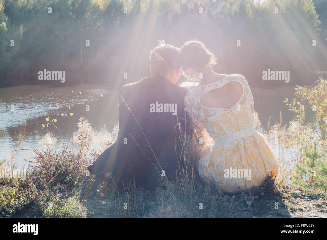 Back view of lovers sitting at water's edge Stock Photo - Alamy