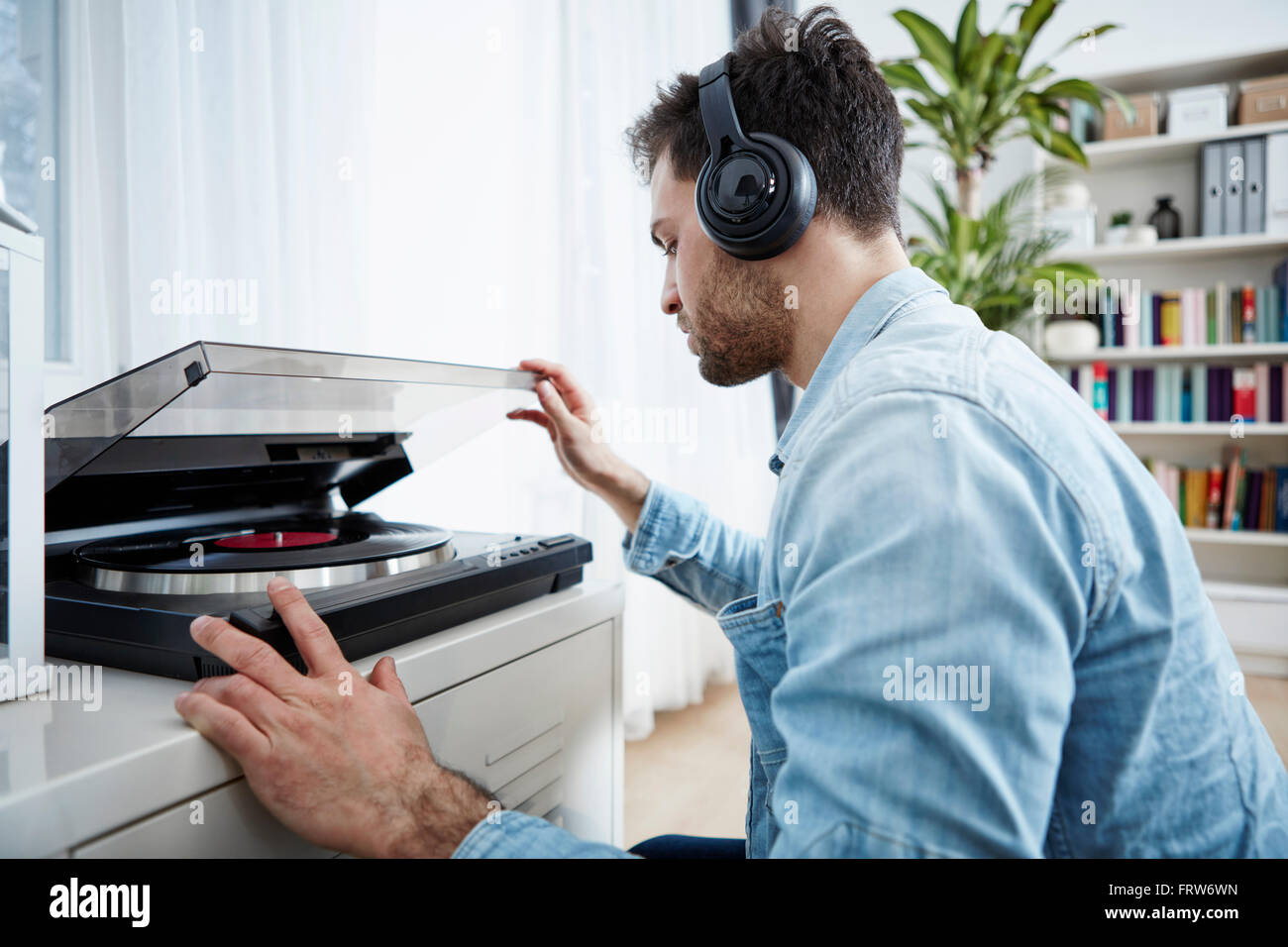 Young man wearing headphones starting record player Stock Photo - Alamy