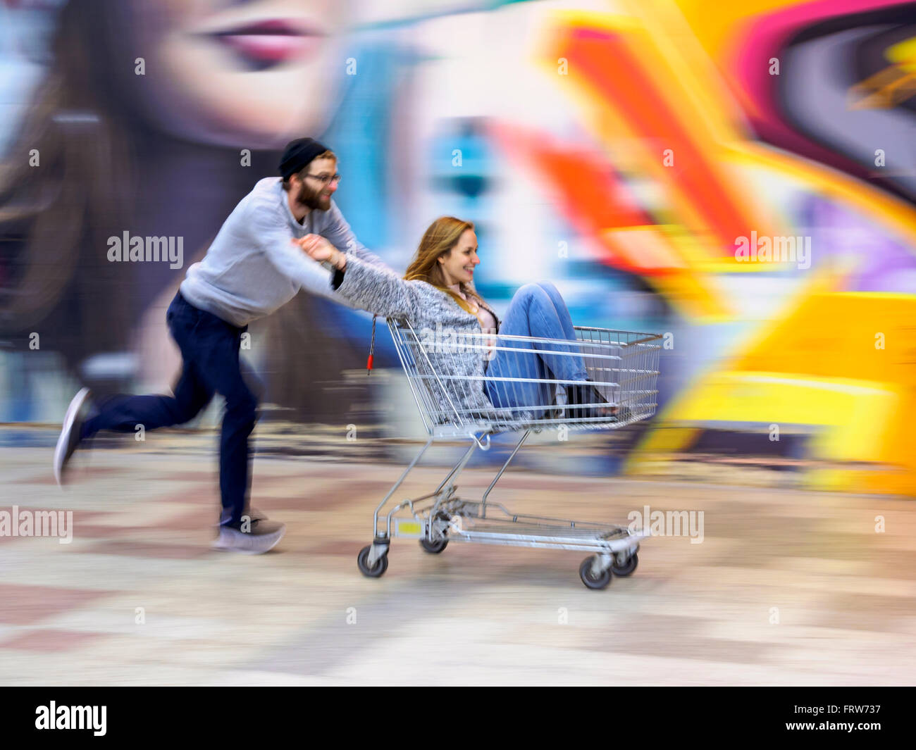 Young man pushing woman in shopping cart, laughing and running Stock ...
