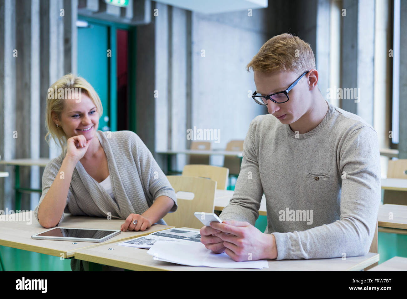 Two students in classroom with man using cell phone Stock Photo - Alamy