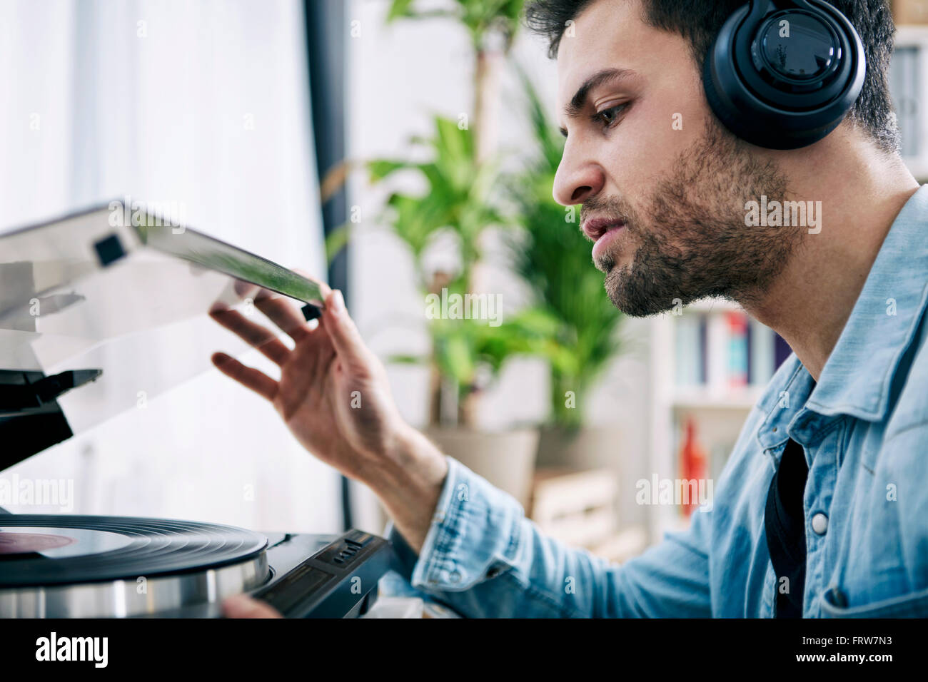 Young man wearing headphones starting record player Stock Photo - Alamy
