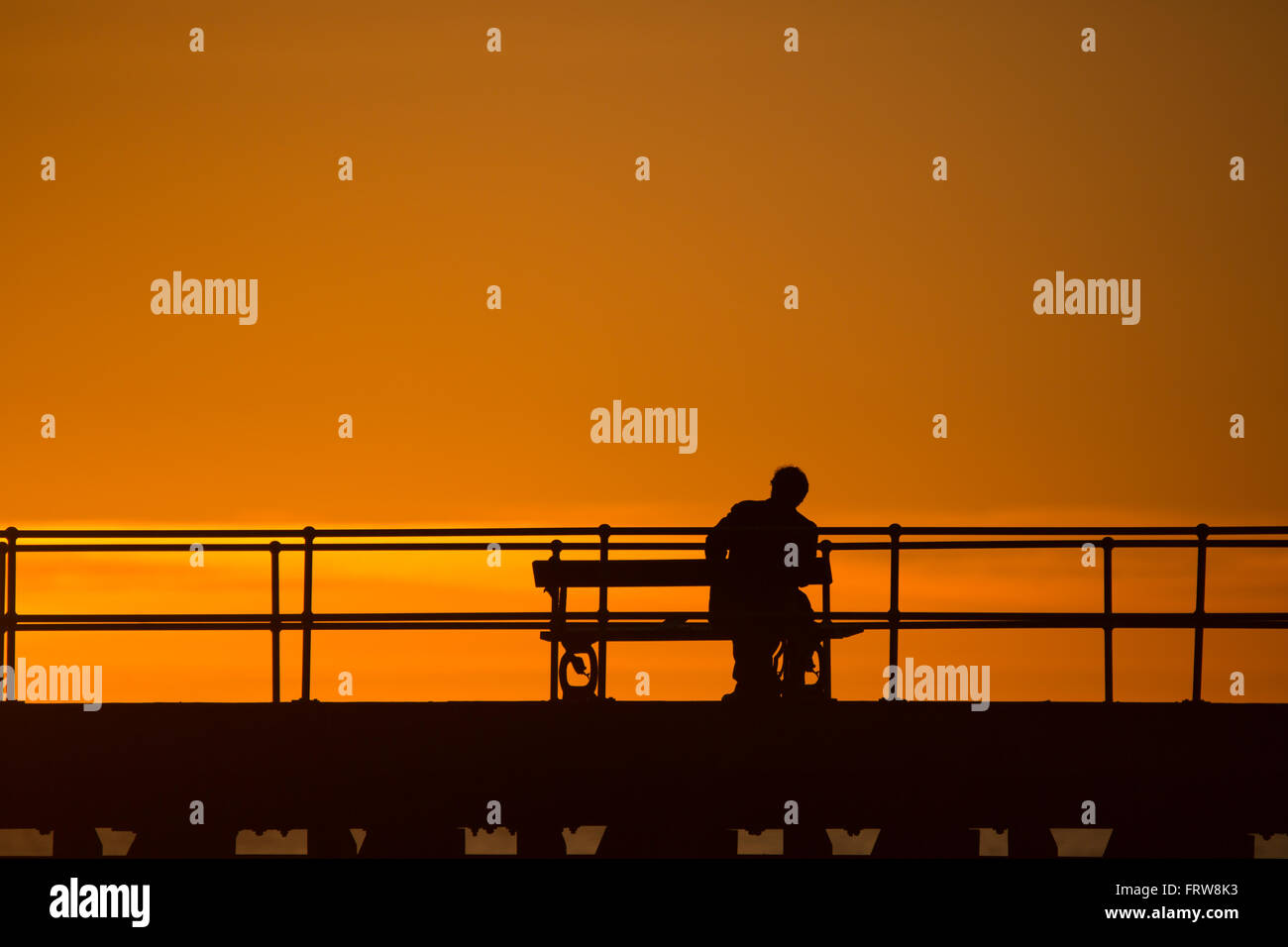 A man sitting on a bench watching the sun go down Stock Photo - Alamy