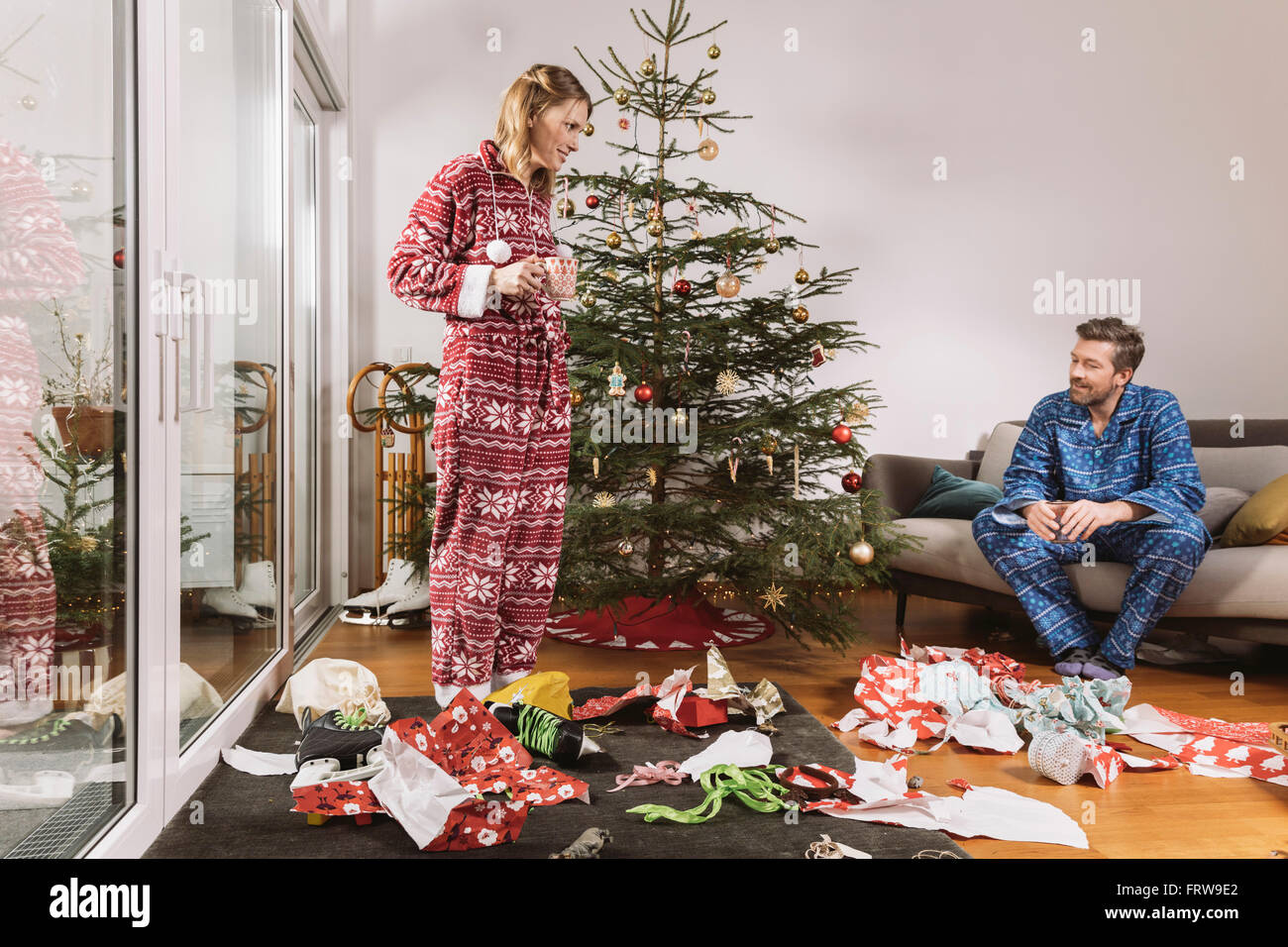 Tired couple in Christmas pyjamas looking at mess of wrapping paper ...