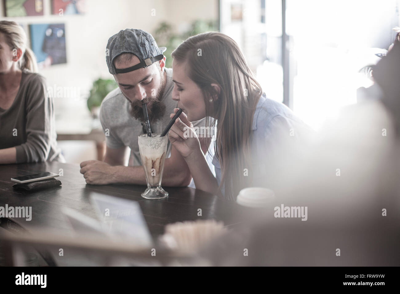 Man and woman sharing milkshake in coffee shop Stock Photo - Alamy
