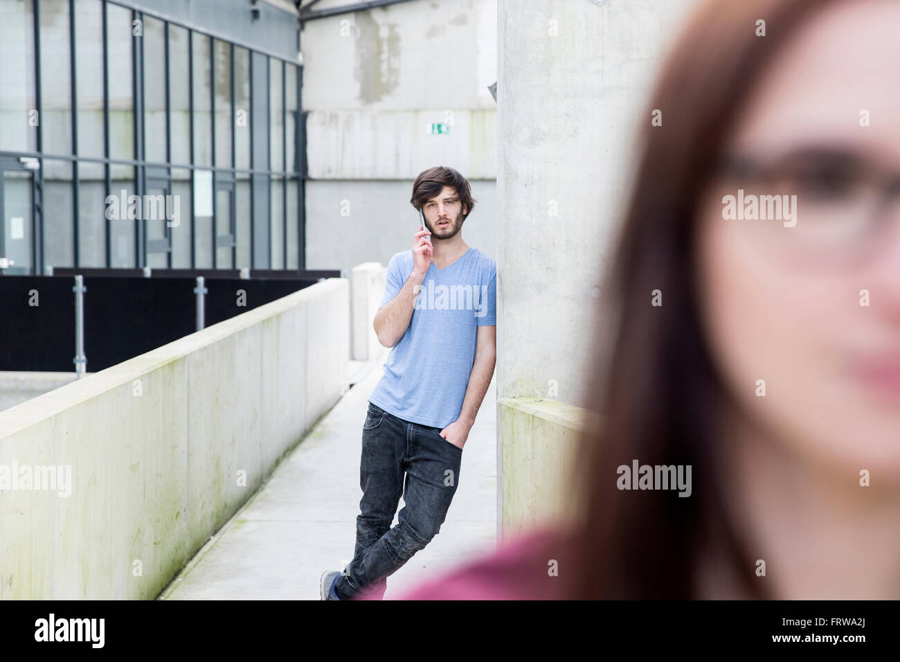 Young man leaning against concrete wall telephoning with smartphone ...