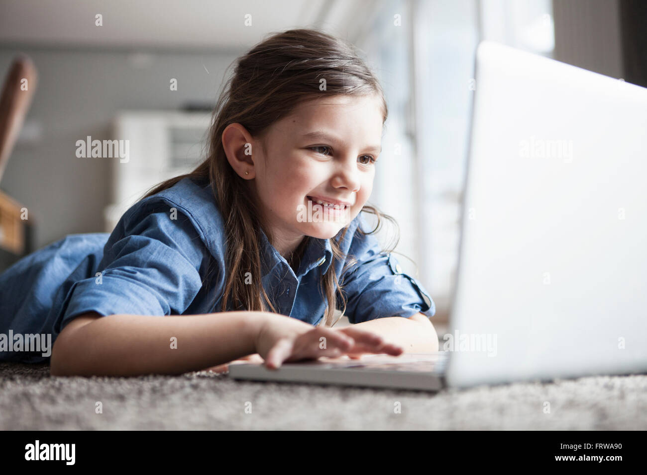 Portrait of smiling little girl lying on the floor using laptop Stock ...